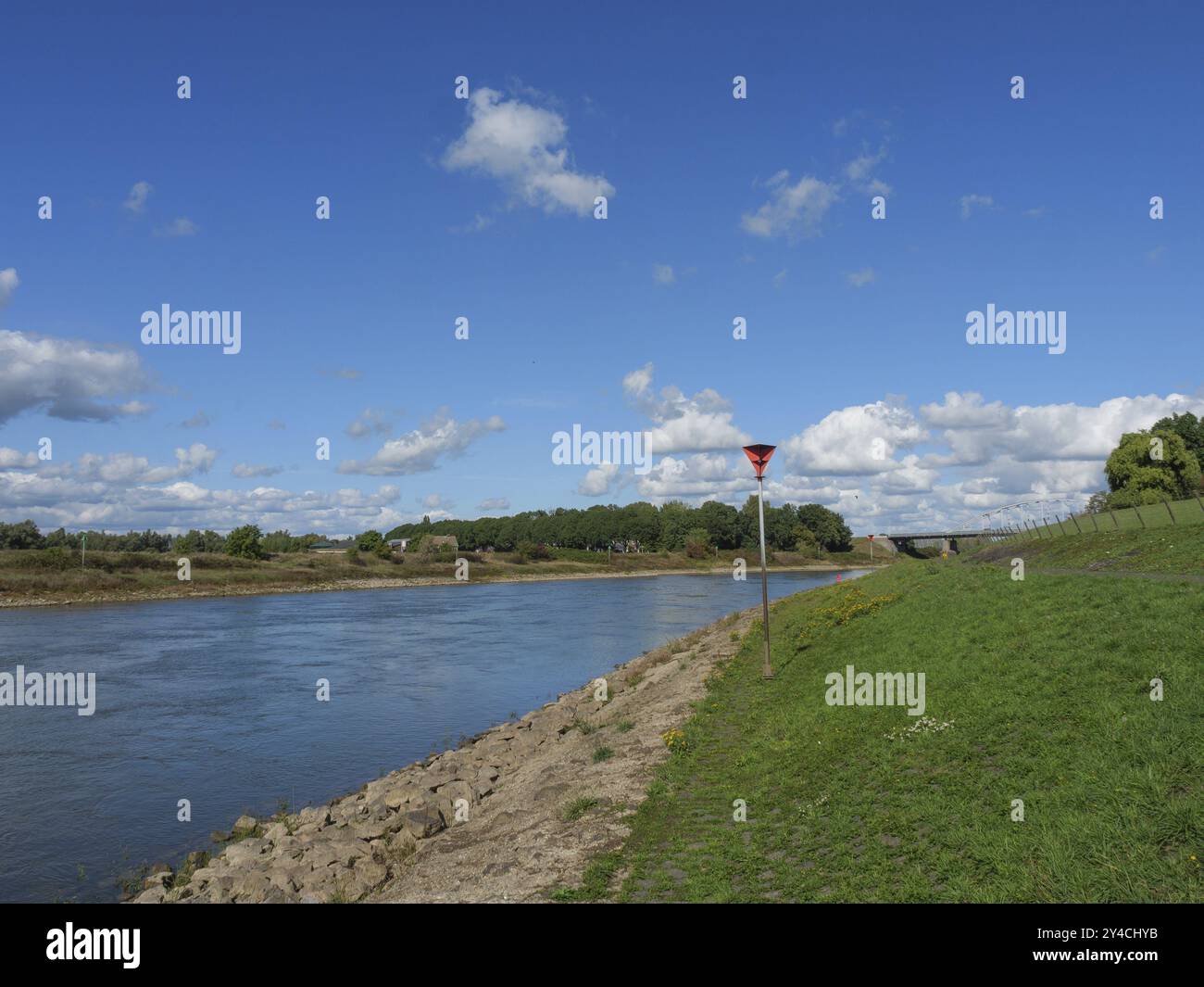 Riverbank with grassy areas and a marked sign under a clear sky ...
