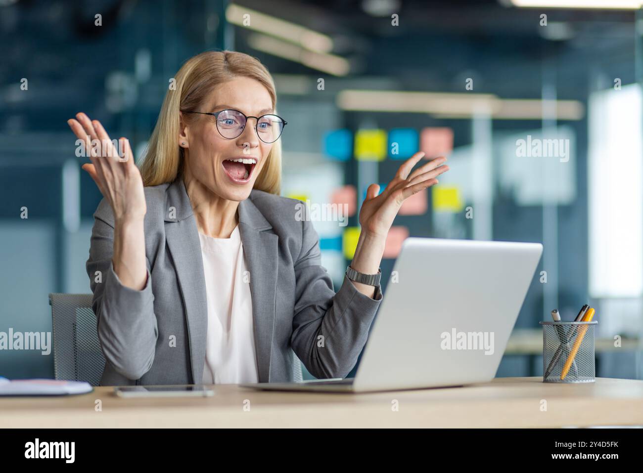 Joyful businesswoman expressing excitement at office desk with laptop ...