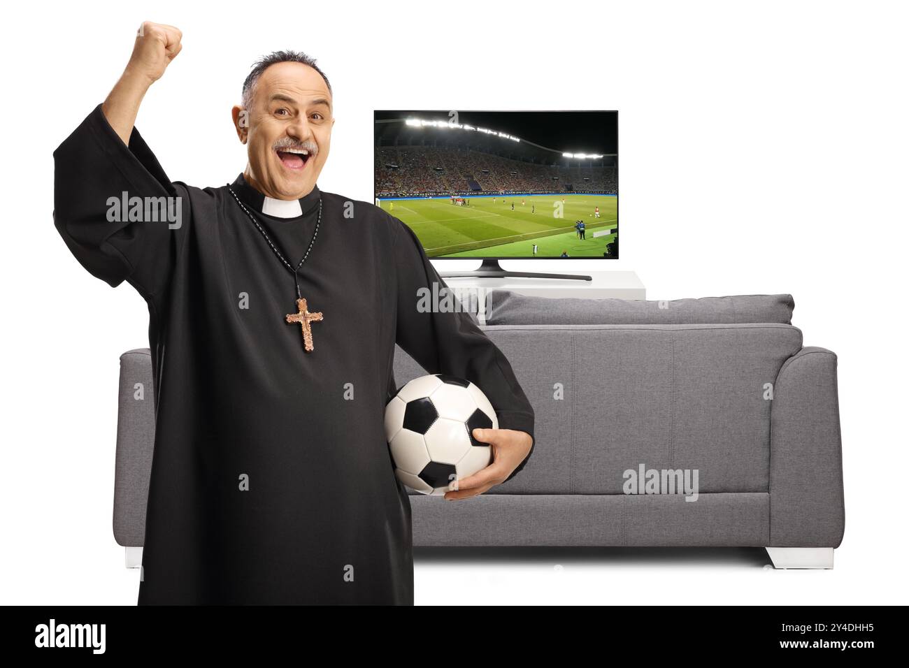 Happy priest holding a football and cheering in front of tv and sofa ...