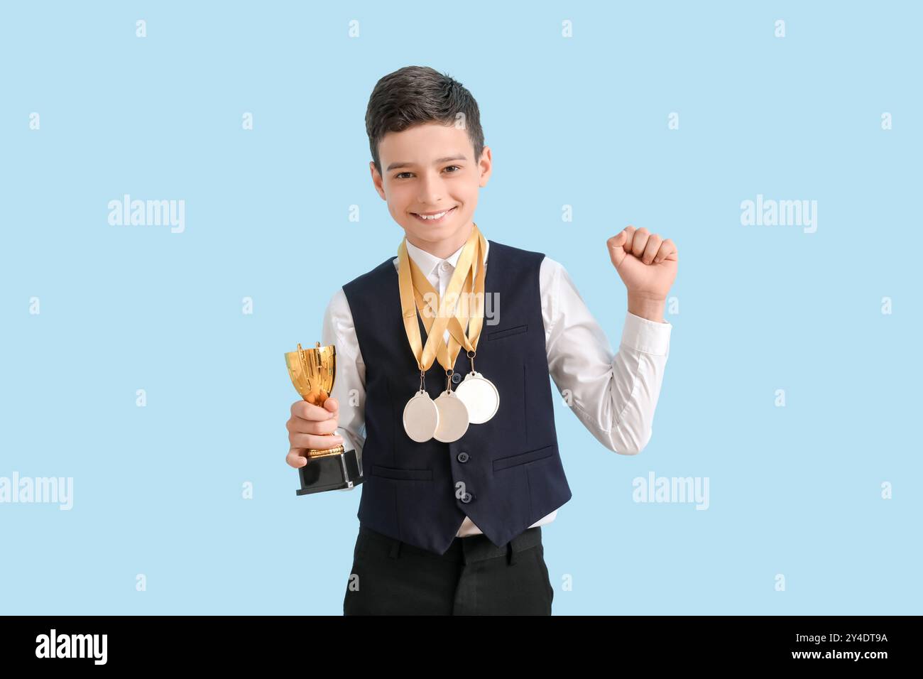 Smart little school boy with prize cup and medals on light blue ...