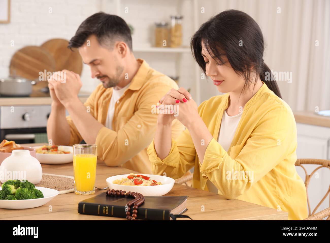 Religious young woman with her husband praying before dinner at table ...