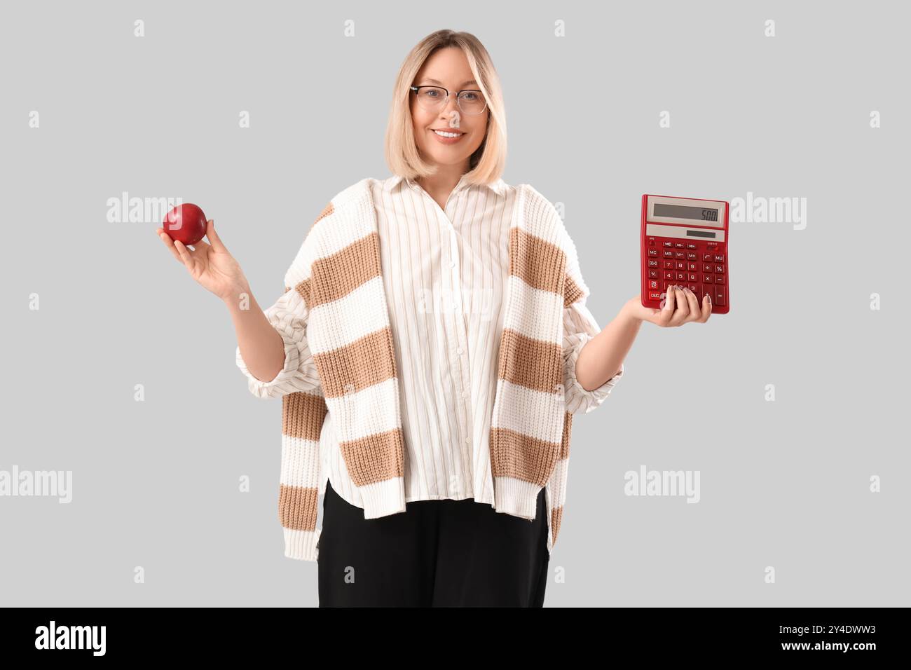 Mature female math teacher with calculator and apple on grey background ...