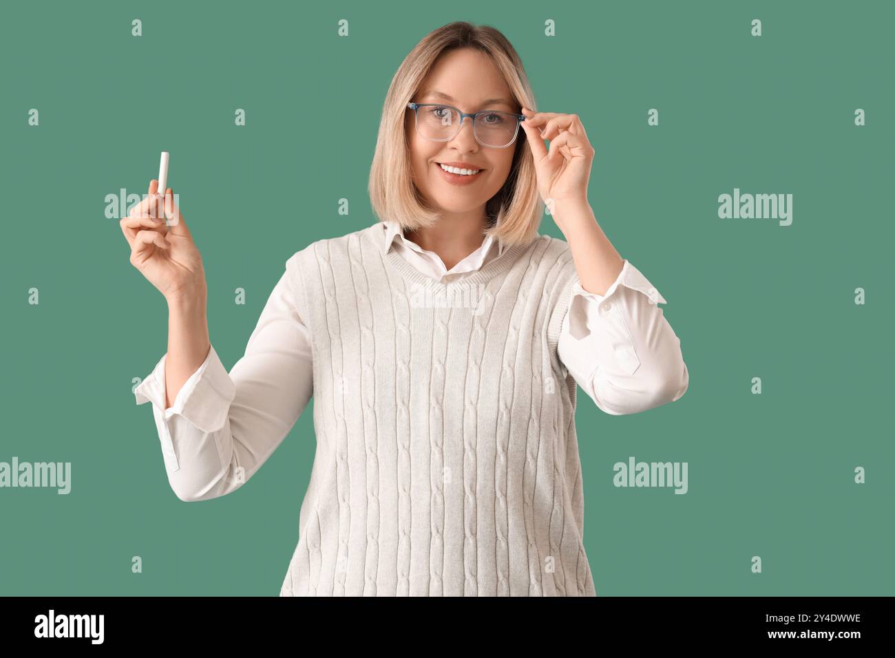 Mature female math teacher holding chalk on green background Stock ...