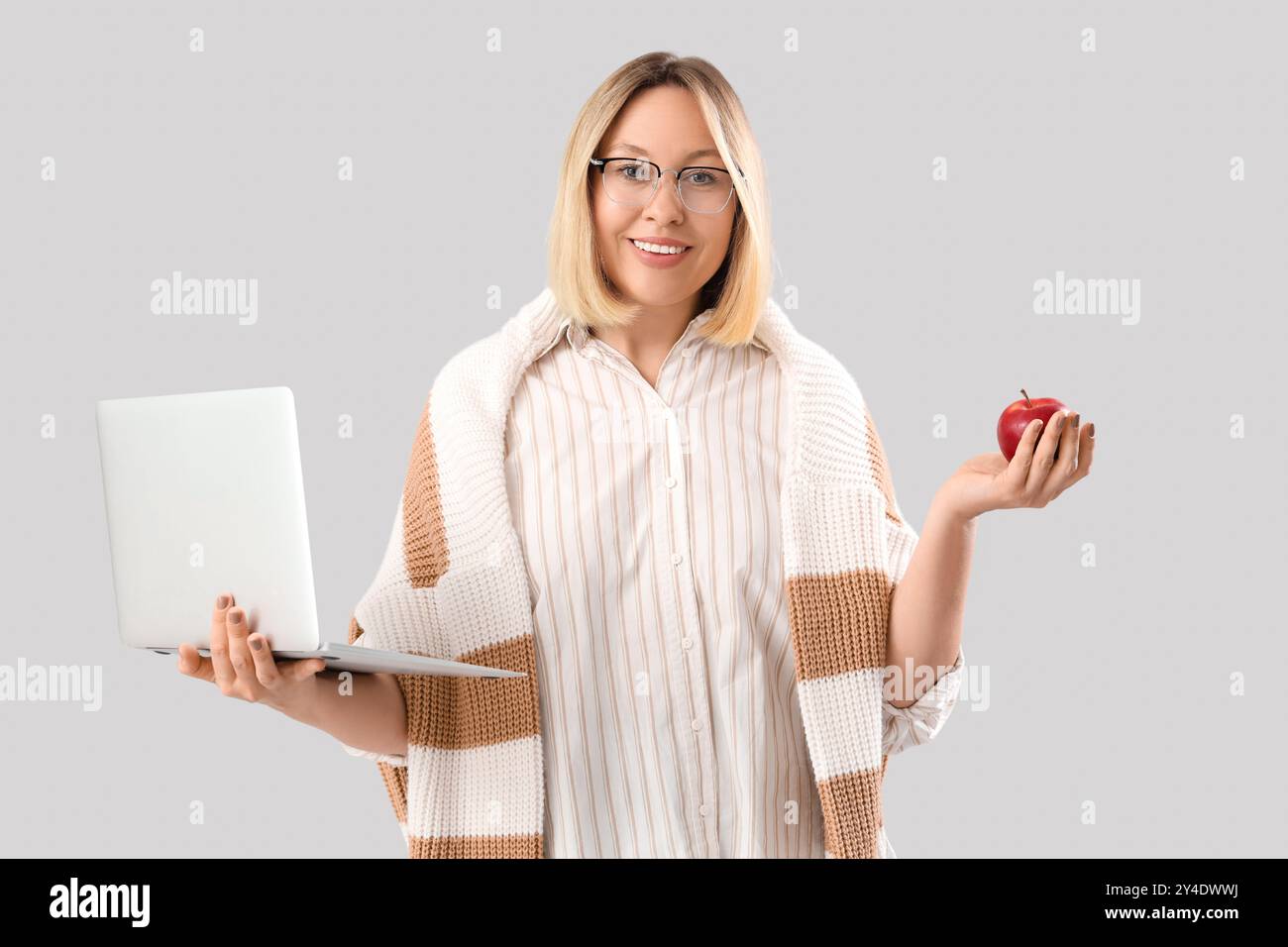 Mature female math teacher with laptop and apple on grey background ...
