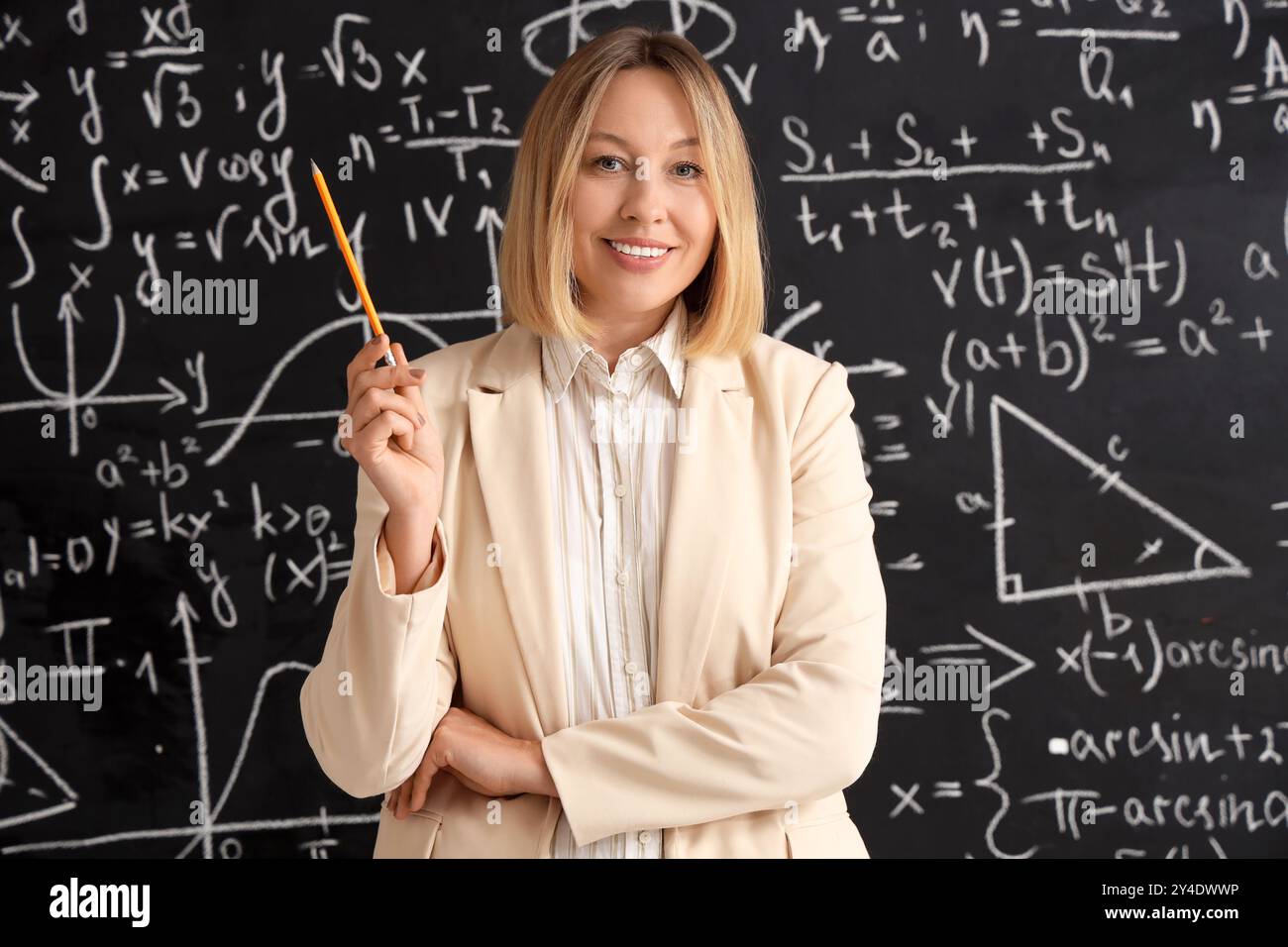 Mature female math teacher with pencil near blackboard in classroom ...