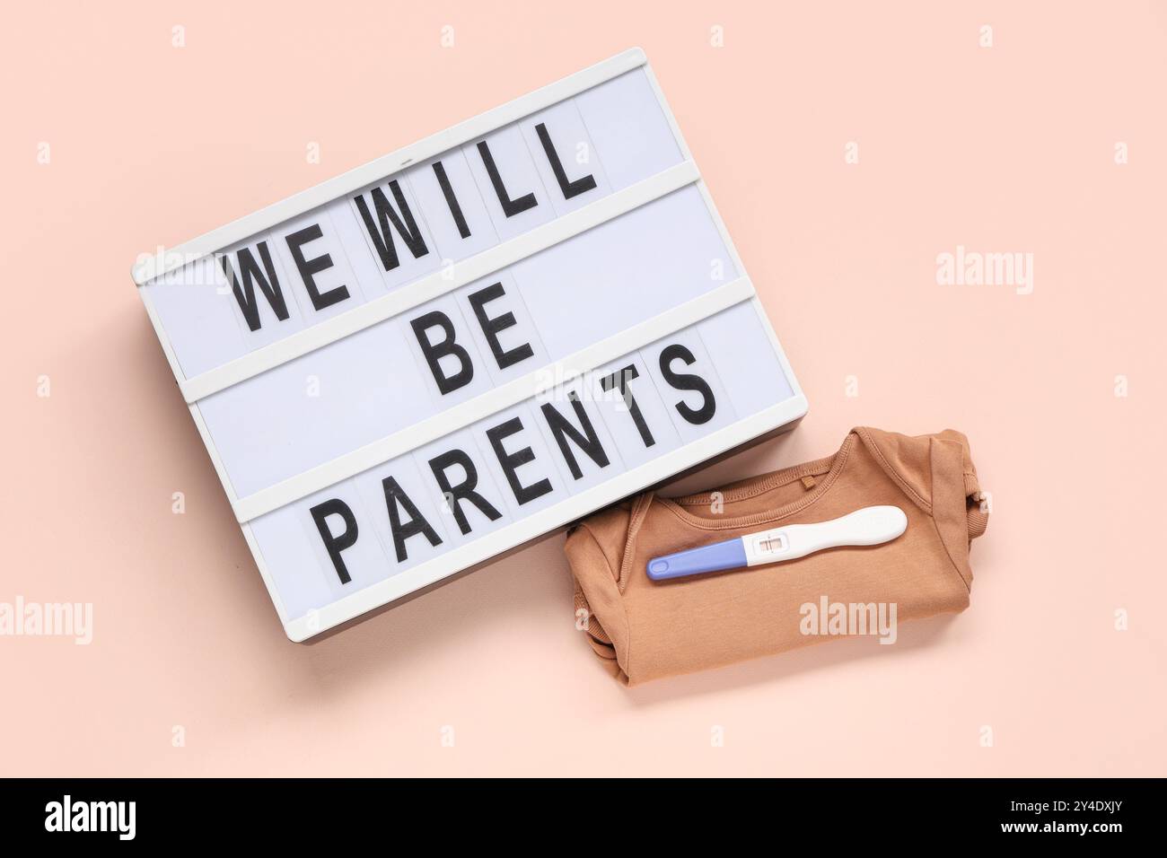 Baby clothes, pregnancy test and board with text WE WILL BE PARENTS on ...