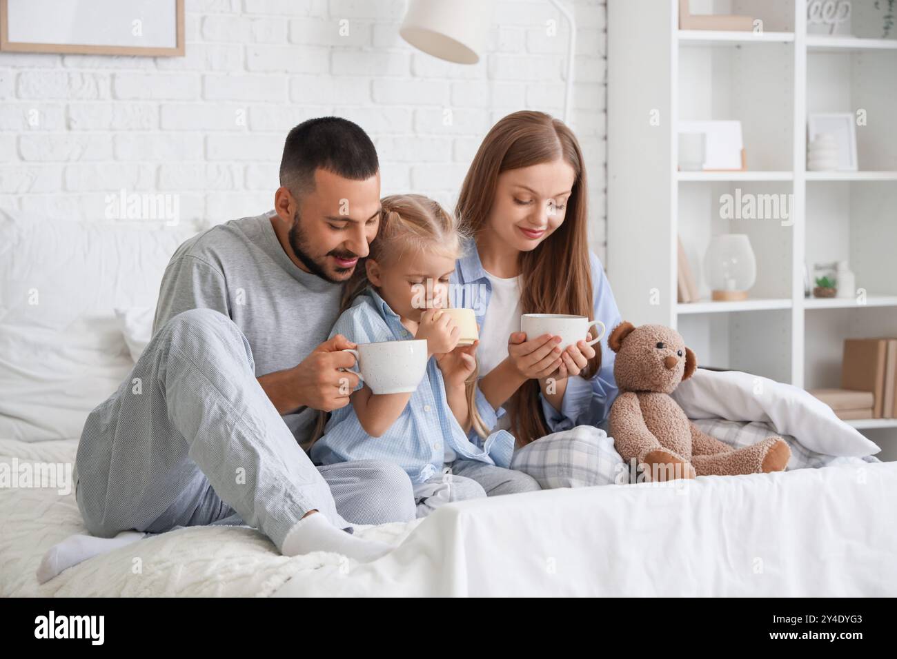 Cute little girl with her parents drinking tea in bedroom Stock Photo ...