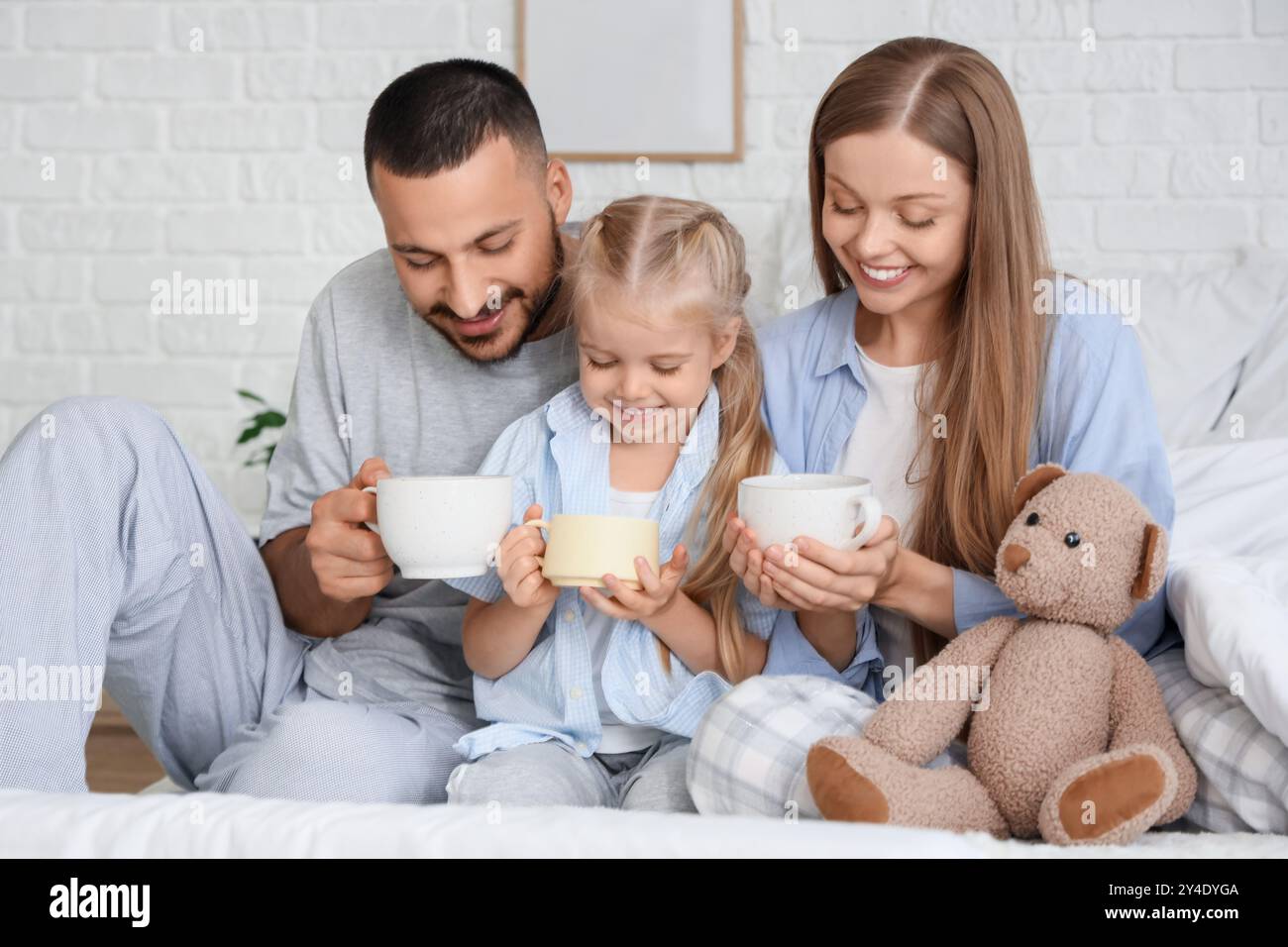 Cute little girl with her parents drinking tea in bedroom Stock Photo ...