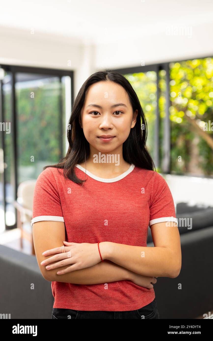 Confident young asian woman standing with arms crossed in modern living ...