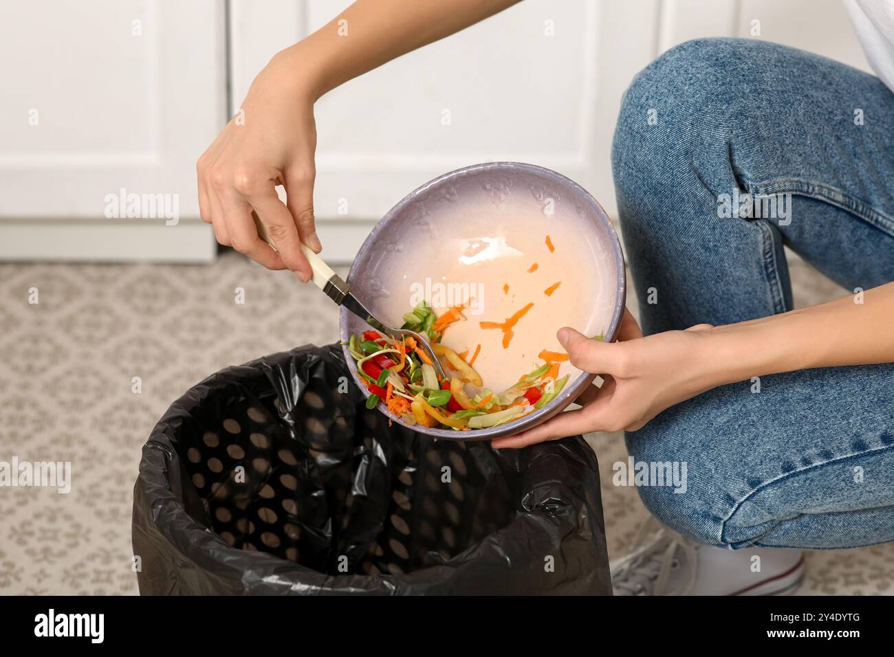 Young woman throwing organic food into trash bin in kitchen, closeup ...