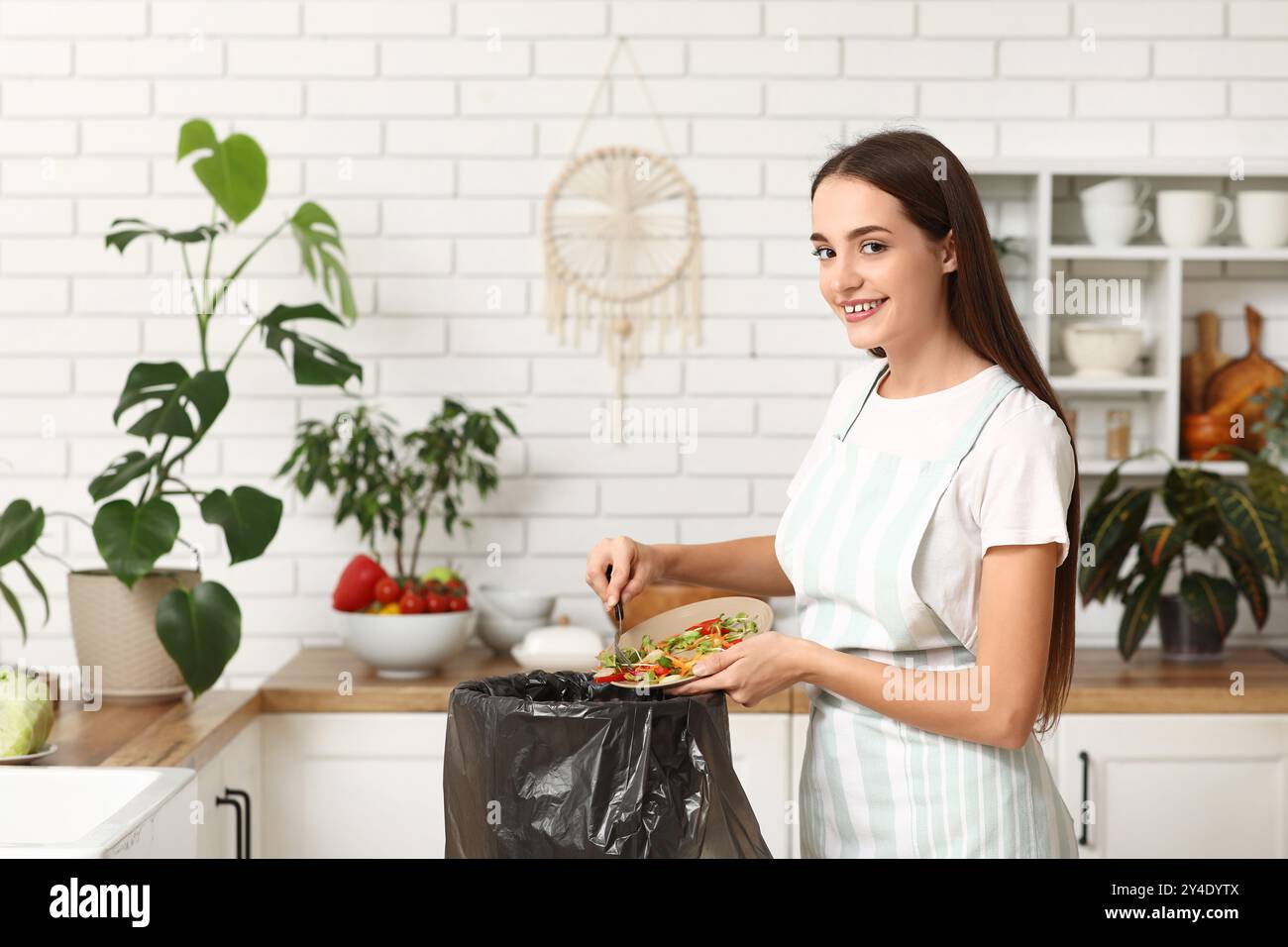 Young woman throwing organic food into trash bin in kitchen. Waste ...