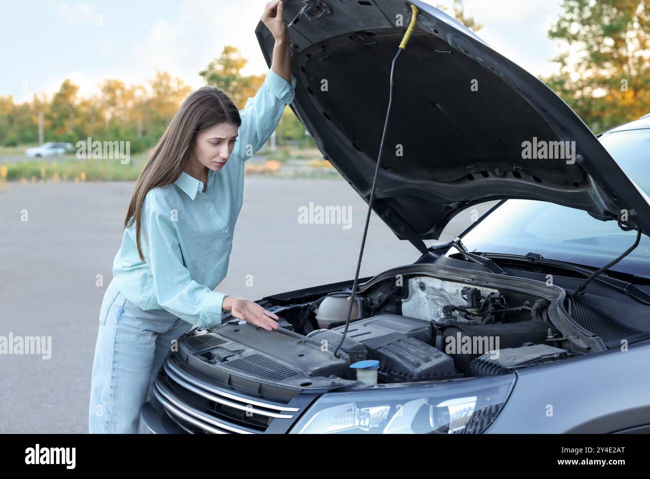 Stressed woman looking under hood of broken car outdoors Stock Photo - Alamy
