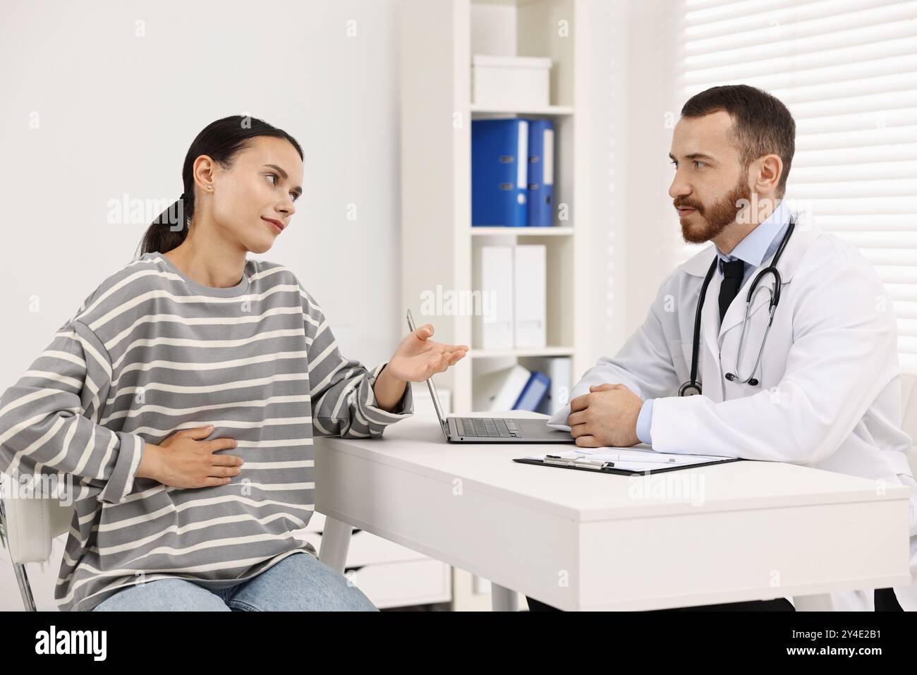 Doctor consulting patient with stomach pain at table in hospital Stock ...