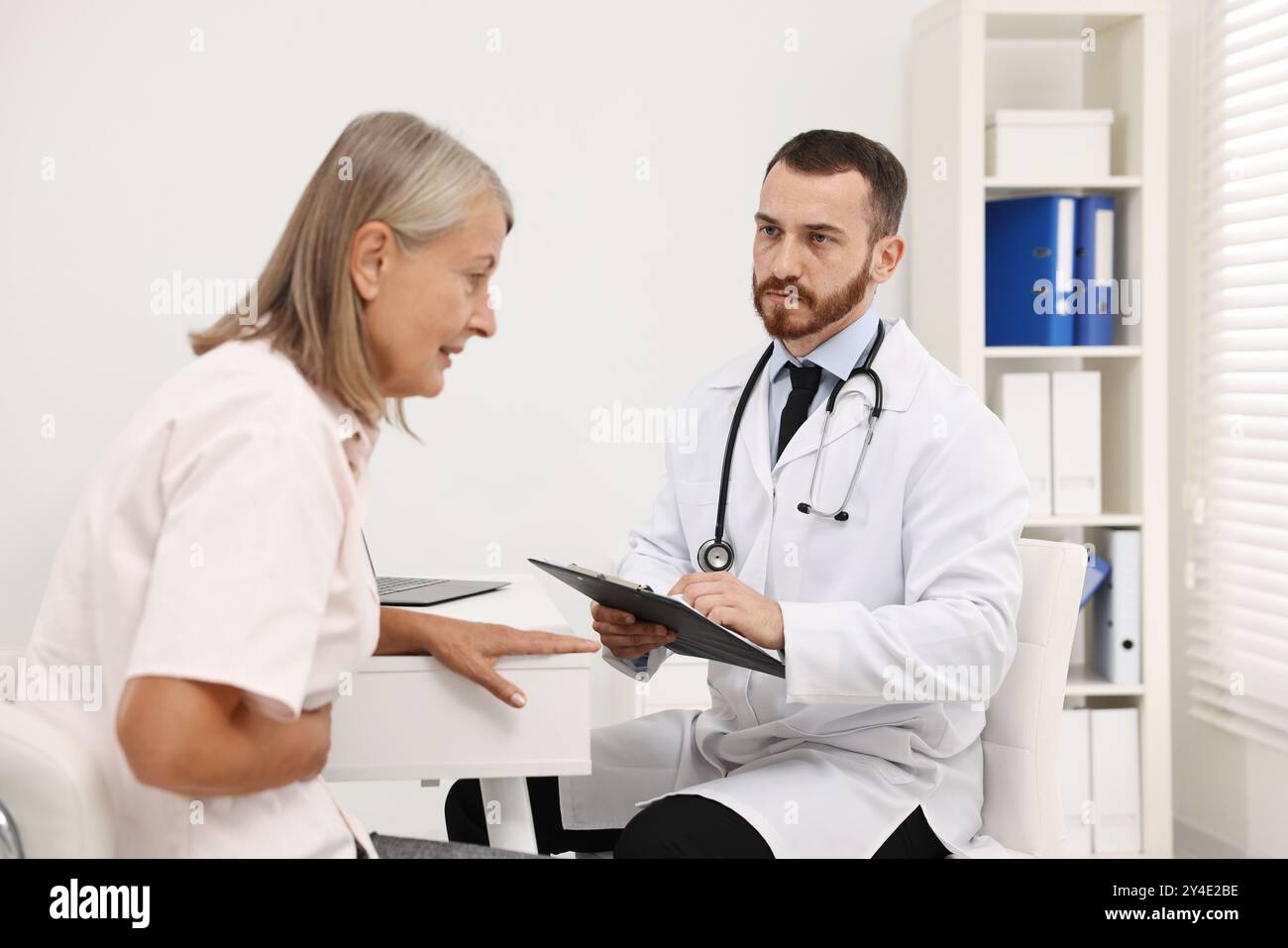 Doctor consulting senior patient with stomach pain at table in hospital ...