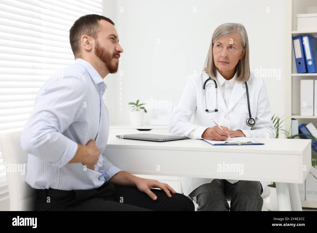 Doctor consulting patient with stomach pain at table in clinic Stock ...
