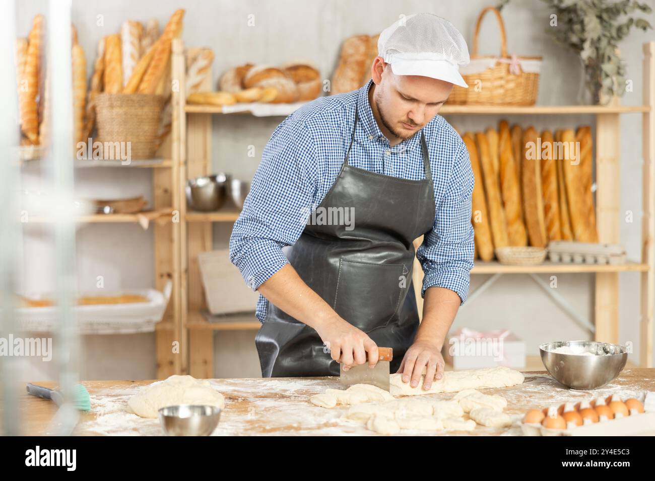 Guy works in bakery as baker, cuts dough into portions, forms pieces of ...