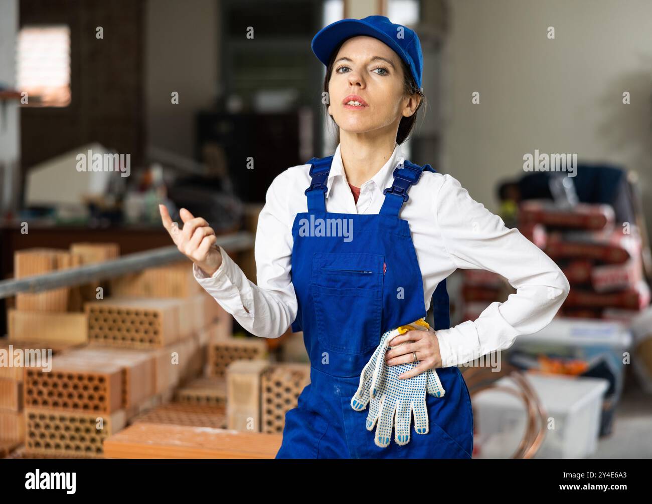 Female builder wearing overalls and cap posing at construction site ...