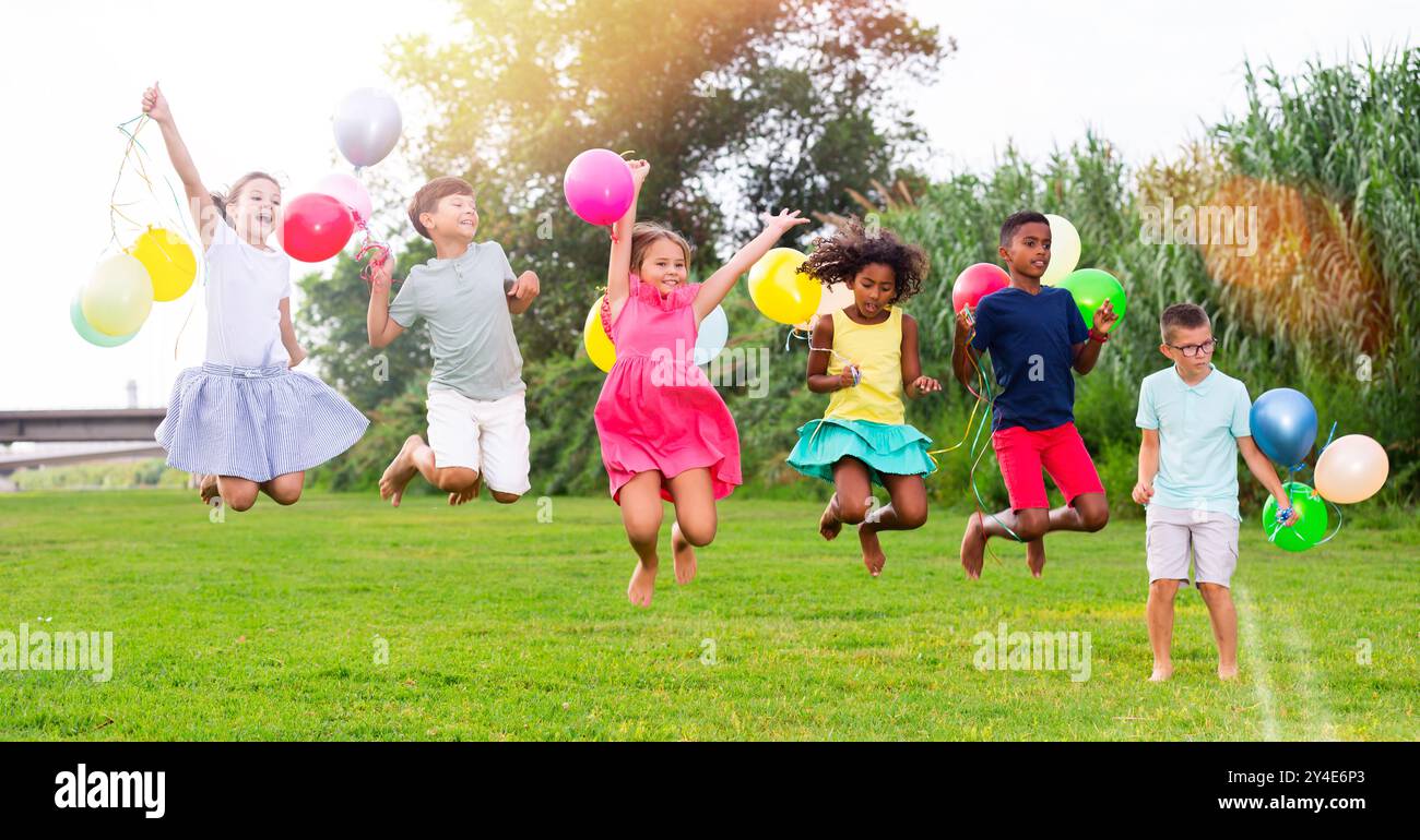 Cheerful tween girls and boys with balloons in hands jumping in summer ...