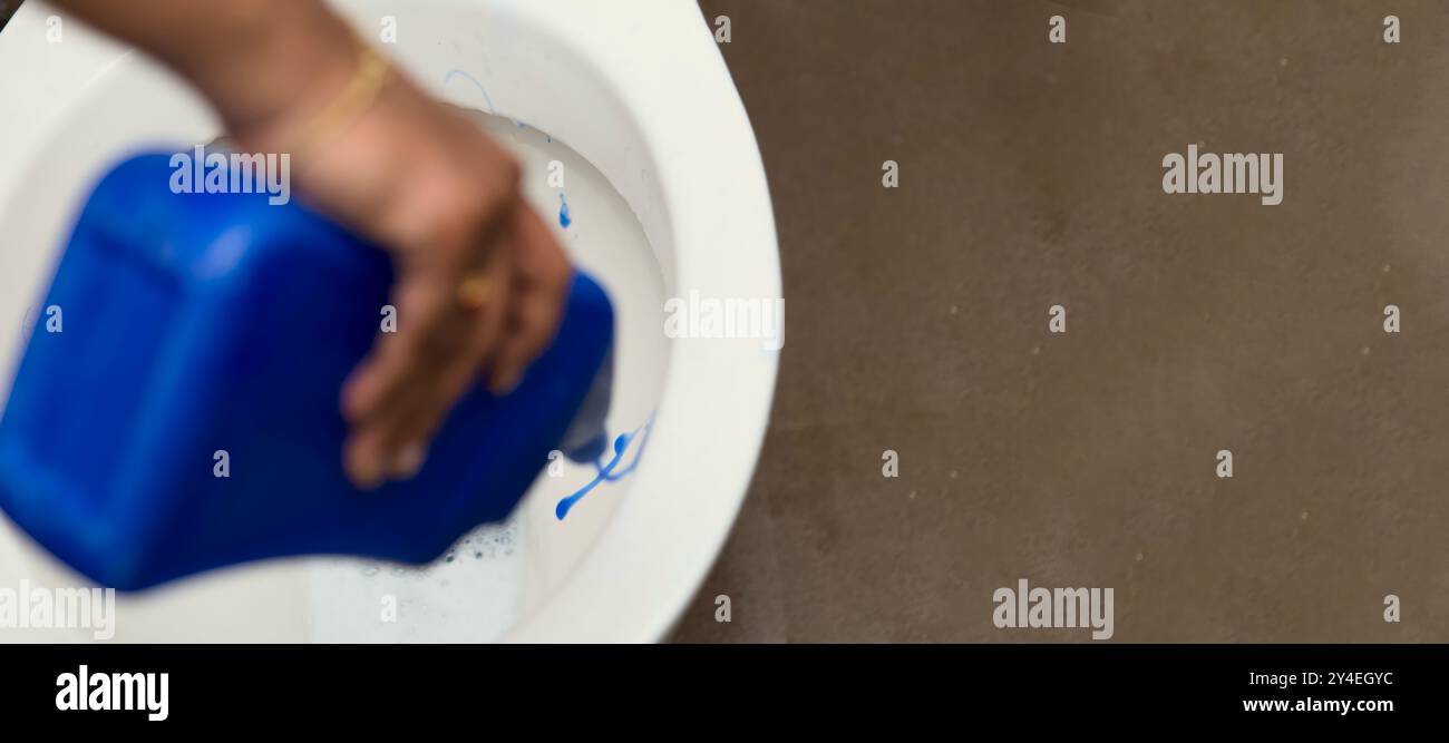 Hand pours blue cleaning fluid into a toilet bowl, ready for a deep ...