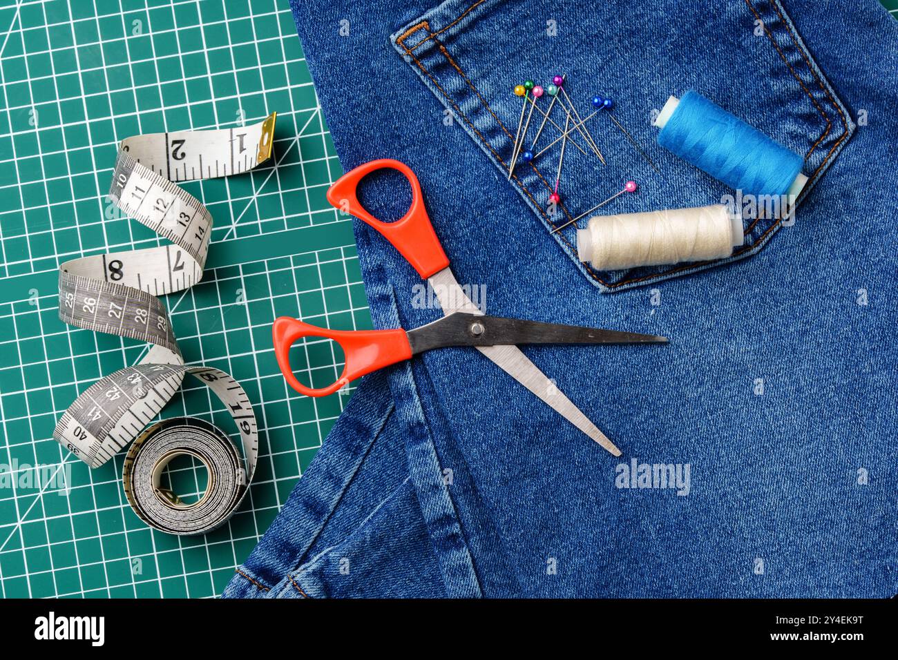 Sewing tools on a cutting mat with denim and thread spools in a craft ...
