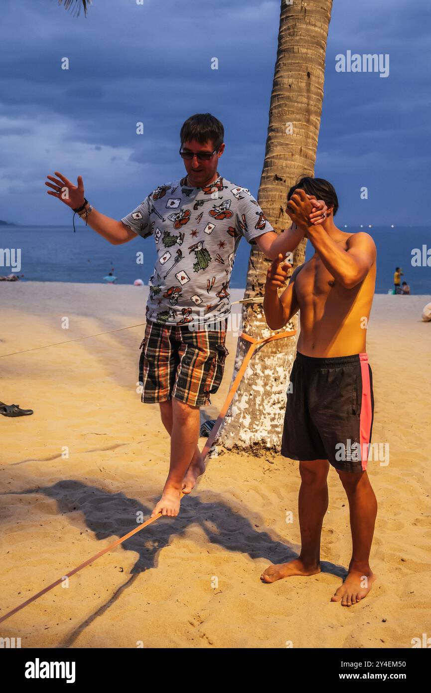 A man learns how to walk a slackline rope in the summer on a beach in ...