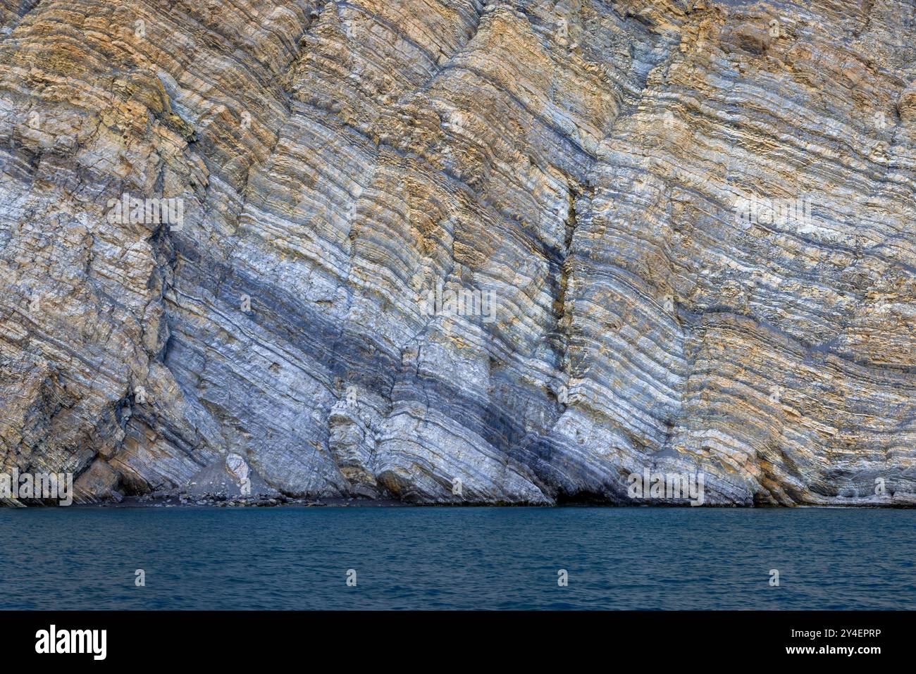The layers of a sedimentary rock cliff rising from the blue waters of ...