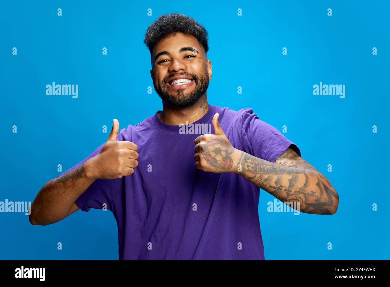 Young man in purple shirt stand against blue background, giving double ...