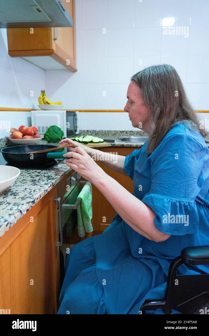 65-year-old woman in a wheelchair cooking in the kitchen of her home ...