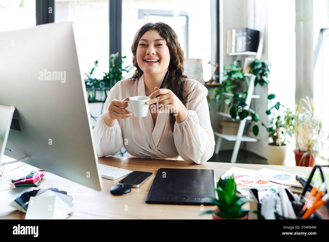 A cheerful young woman sips coffee at her desk, embracing the comfort ...