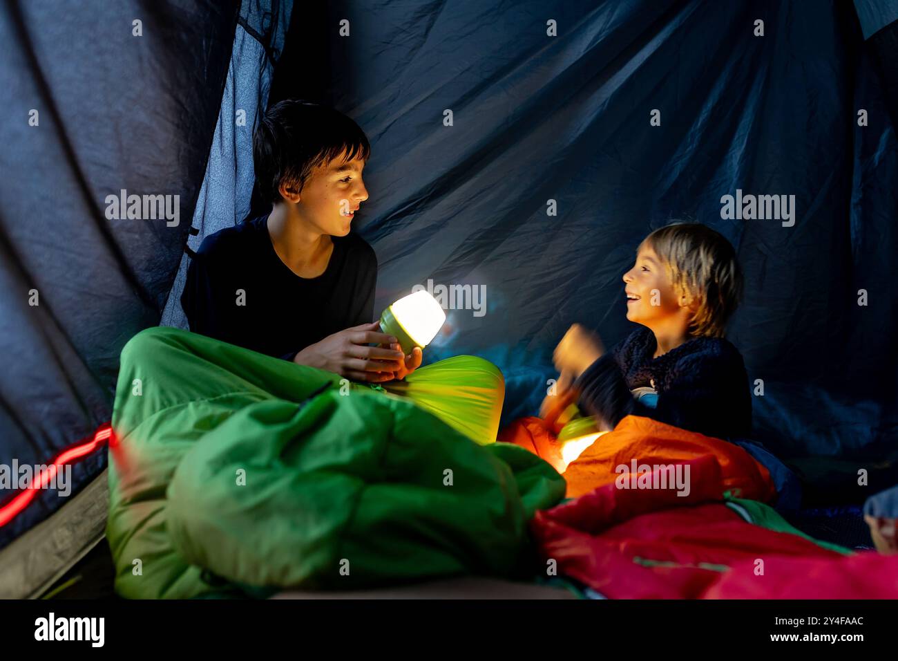 Children, boys siblings, enjoying a night in a tent in camping ...