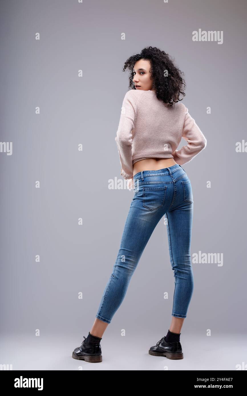 Fashion model with curly hair is standing with her legs apart and hands ...