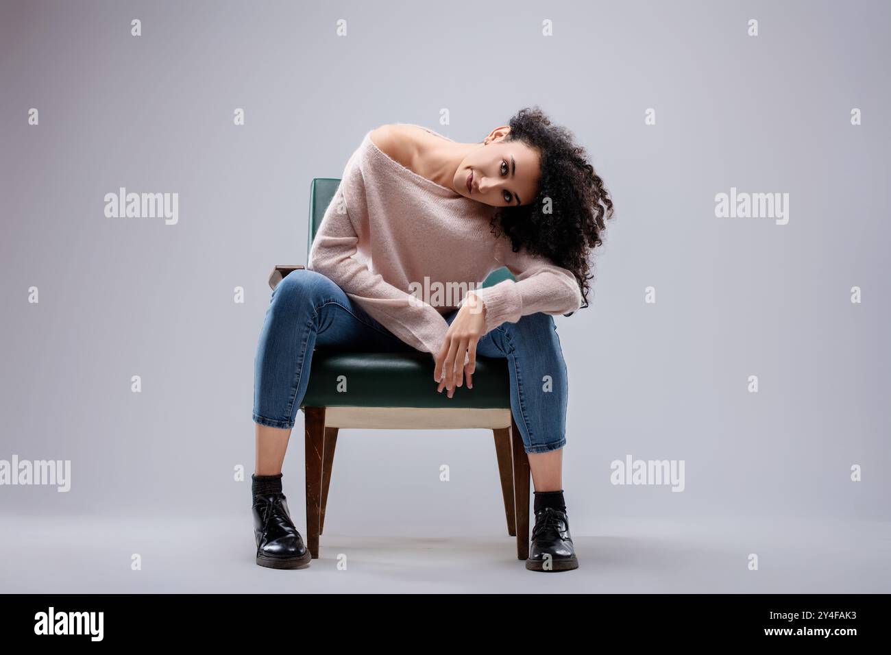 Young woman with curly hair is posing with her legs together and her ...