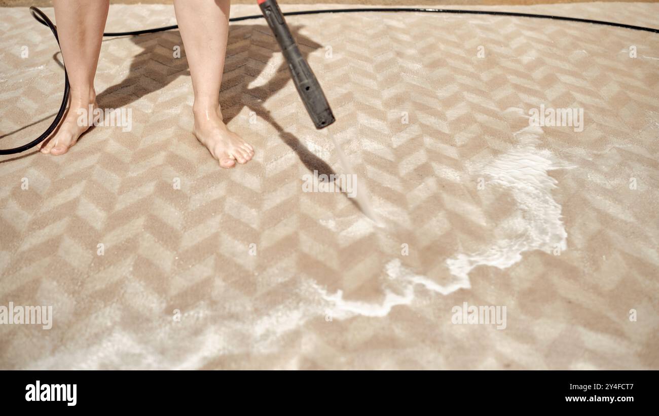 Woman washing carpet with pressure washer, bright sunny day ...