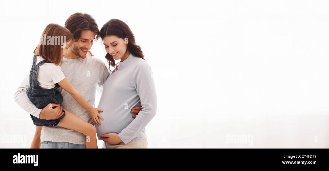 Portrait of happy expecting family with daughter against window at home ...