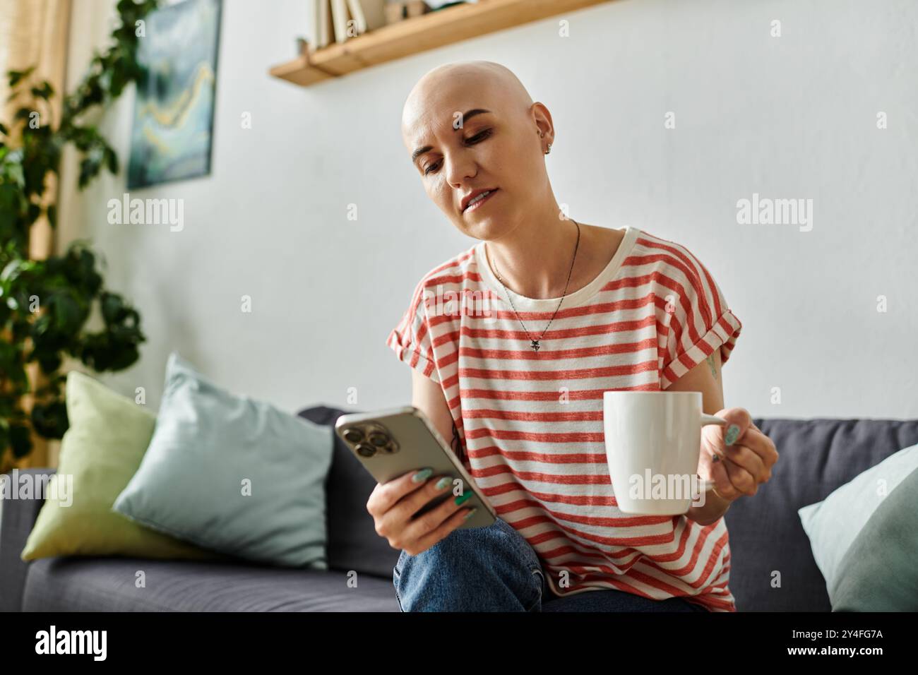A bald woman engages with her phone while relaxing with a cup in a chic ...