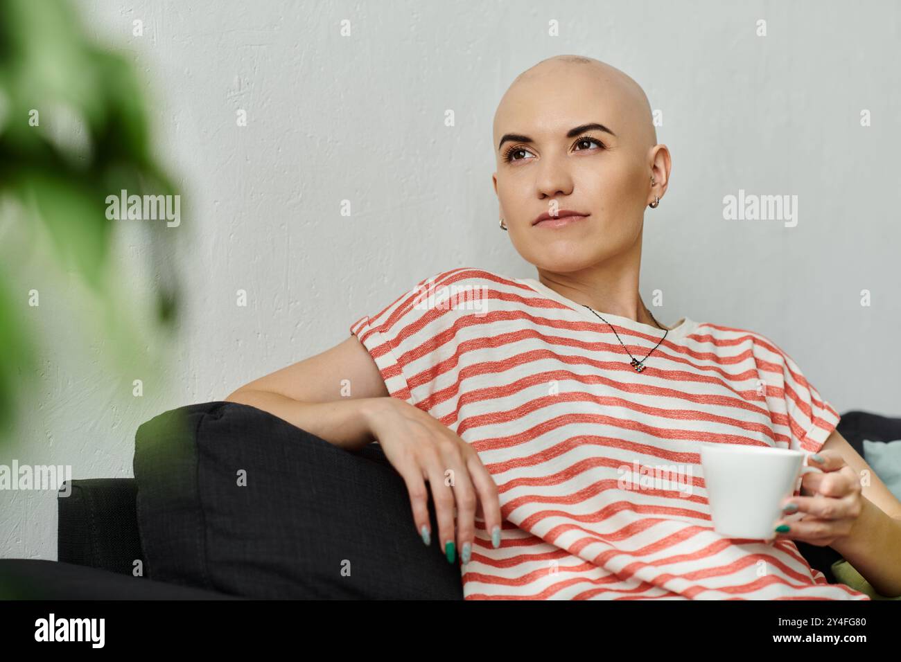 A young bald woman sits comfortably on a couch, enjoying her coffee and ...