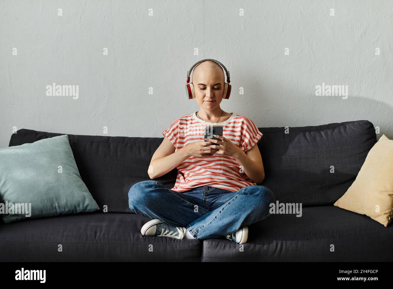 A young, bald woman sits comfortably on a couch, lost in her music with ...