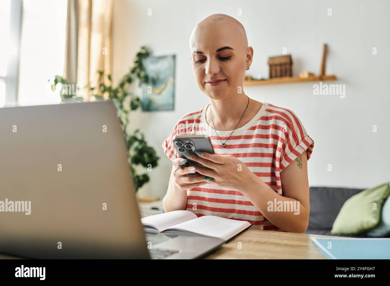 A young woman with alopecia smiles while texting on her phone at a cozy ...