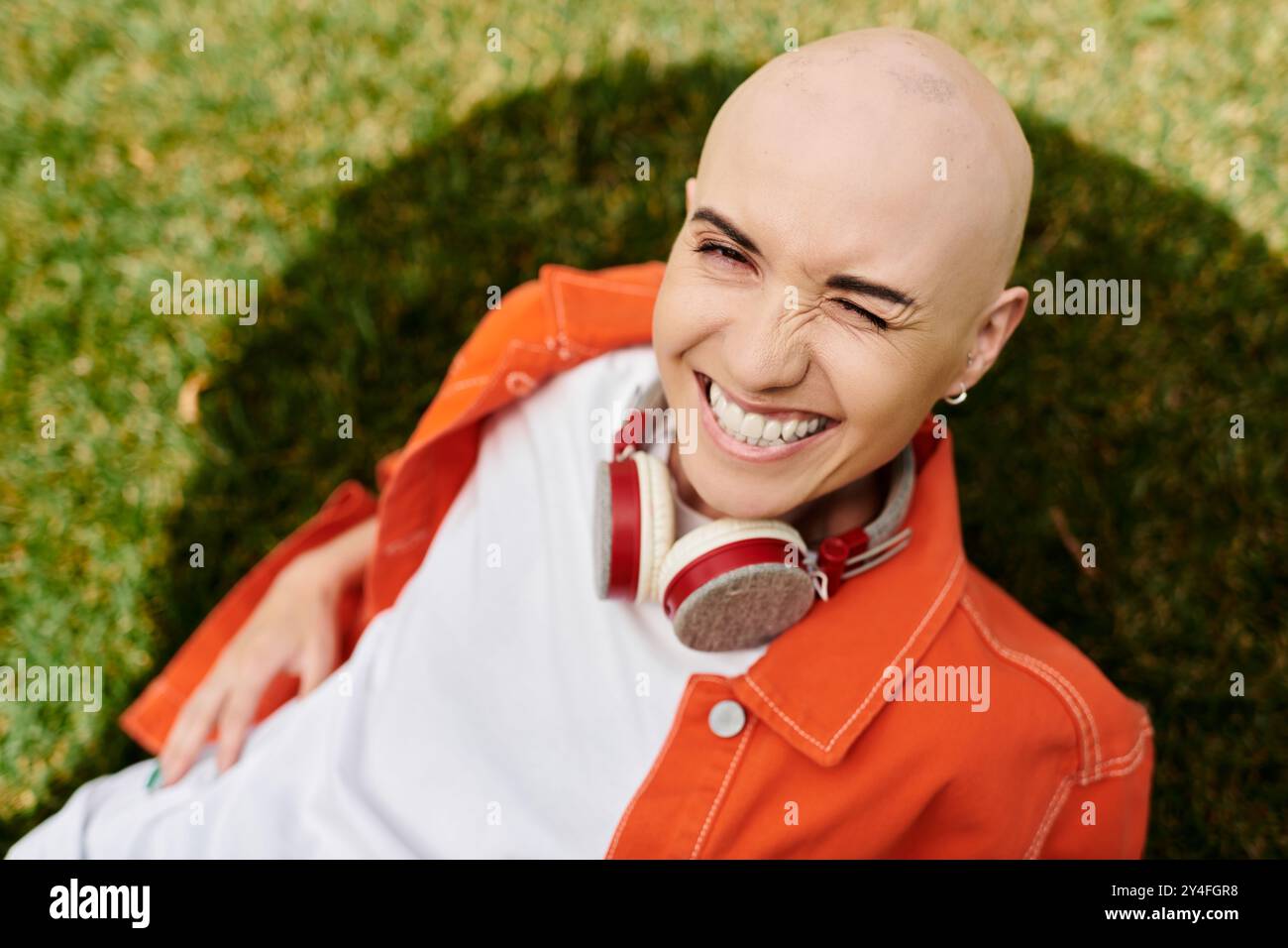 A young bald woman beams a bright smile while relaxing on the grass ...