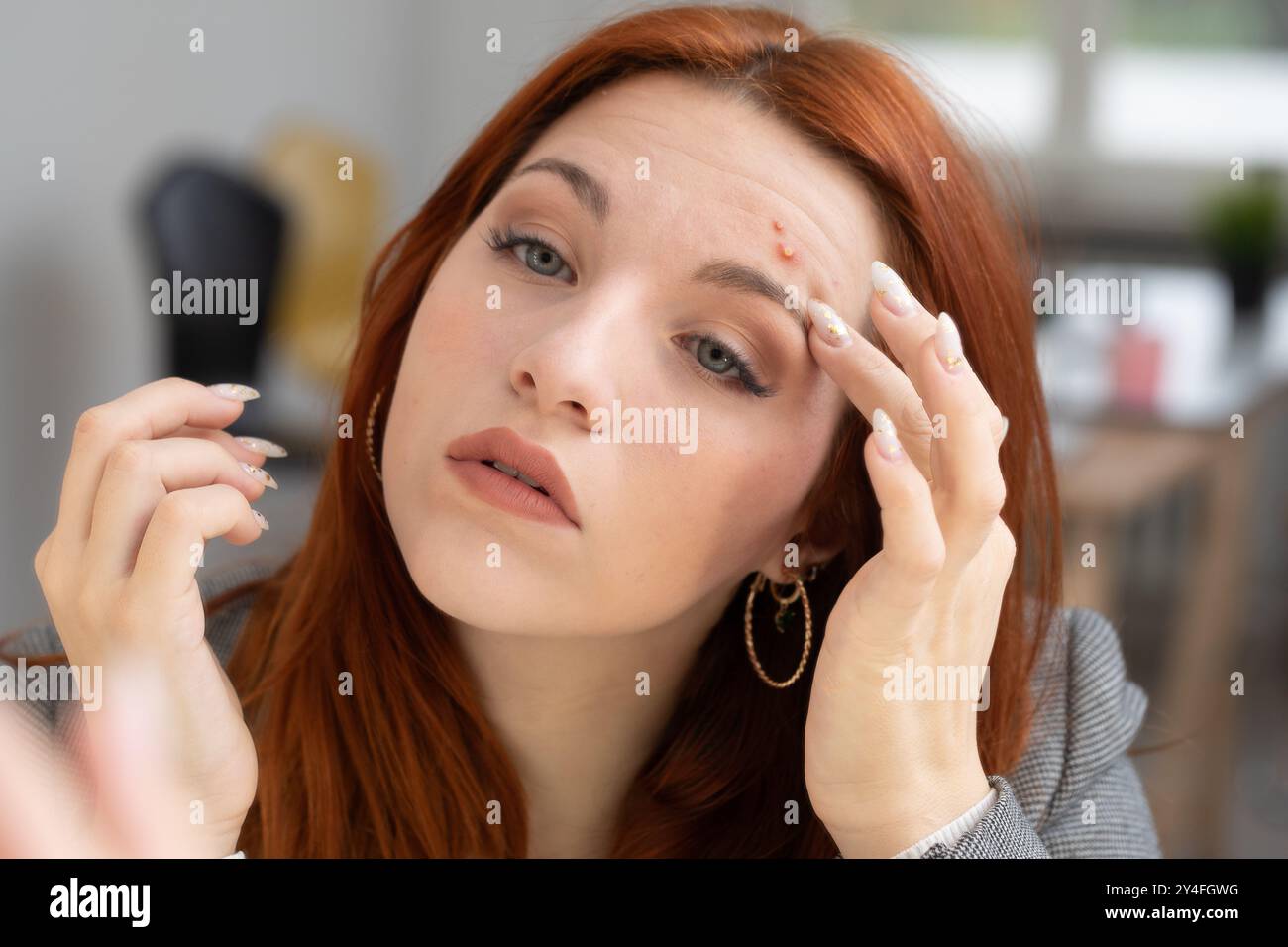 Businesswoman with long red hair is examining her face in the mirror ...