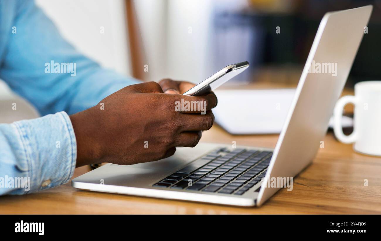Black man typing message on smartphone and working with laptop Stock ...