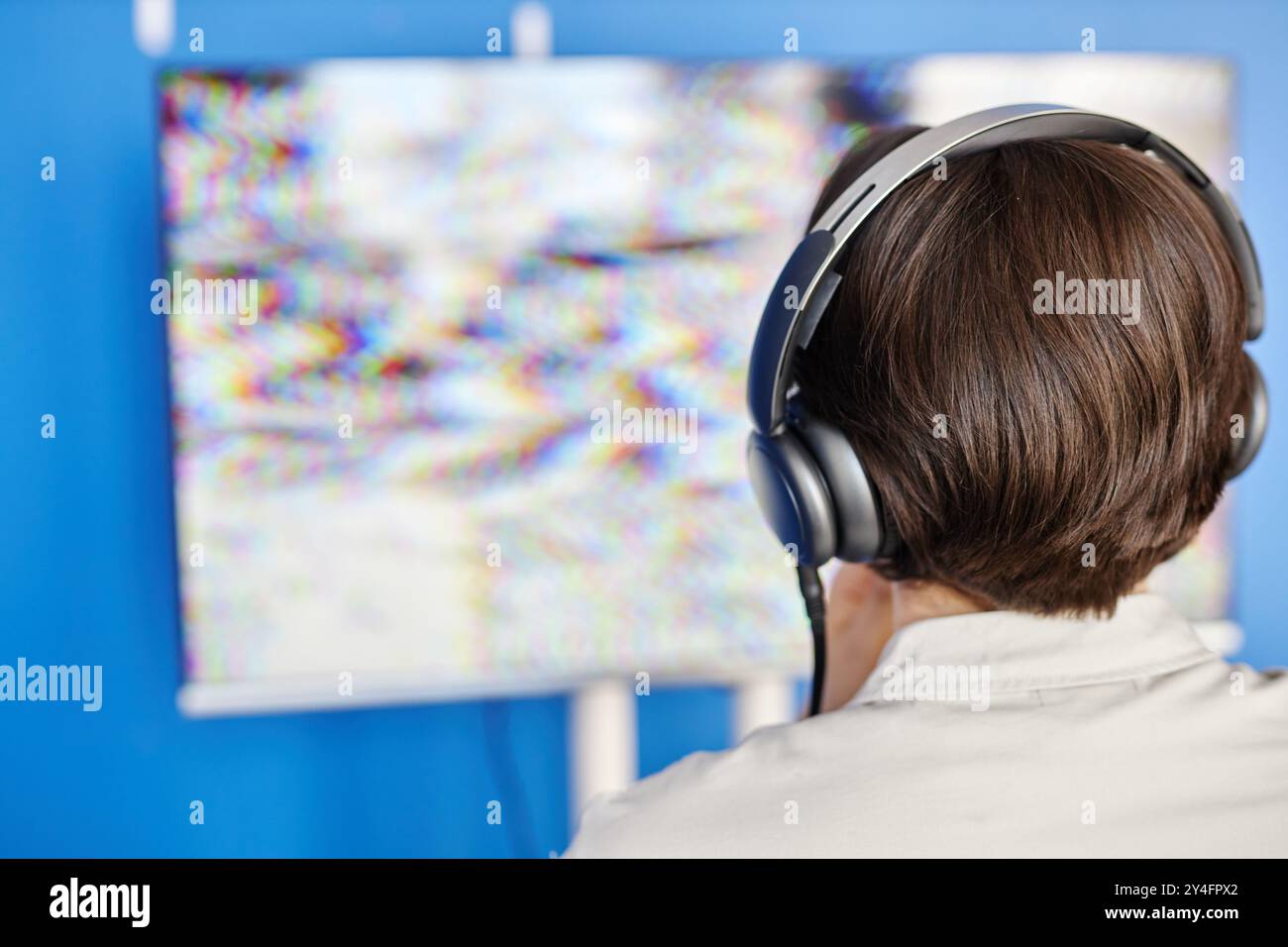 Back view of unrecognizable man wearing headphones looking at TV screen ...
