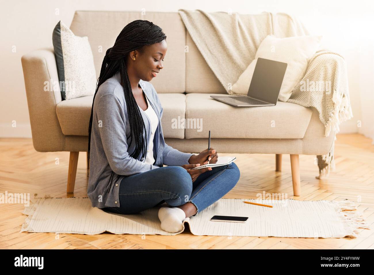 Black female student taking notes while studying at home with laptop ...