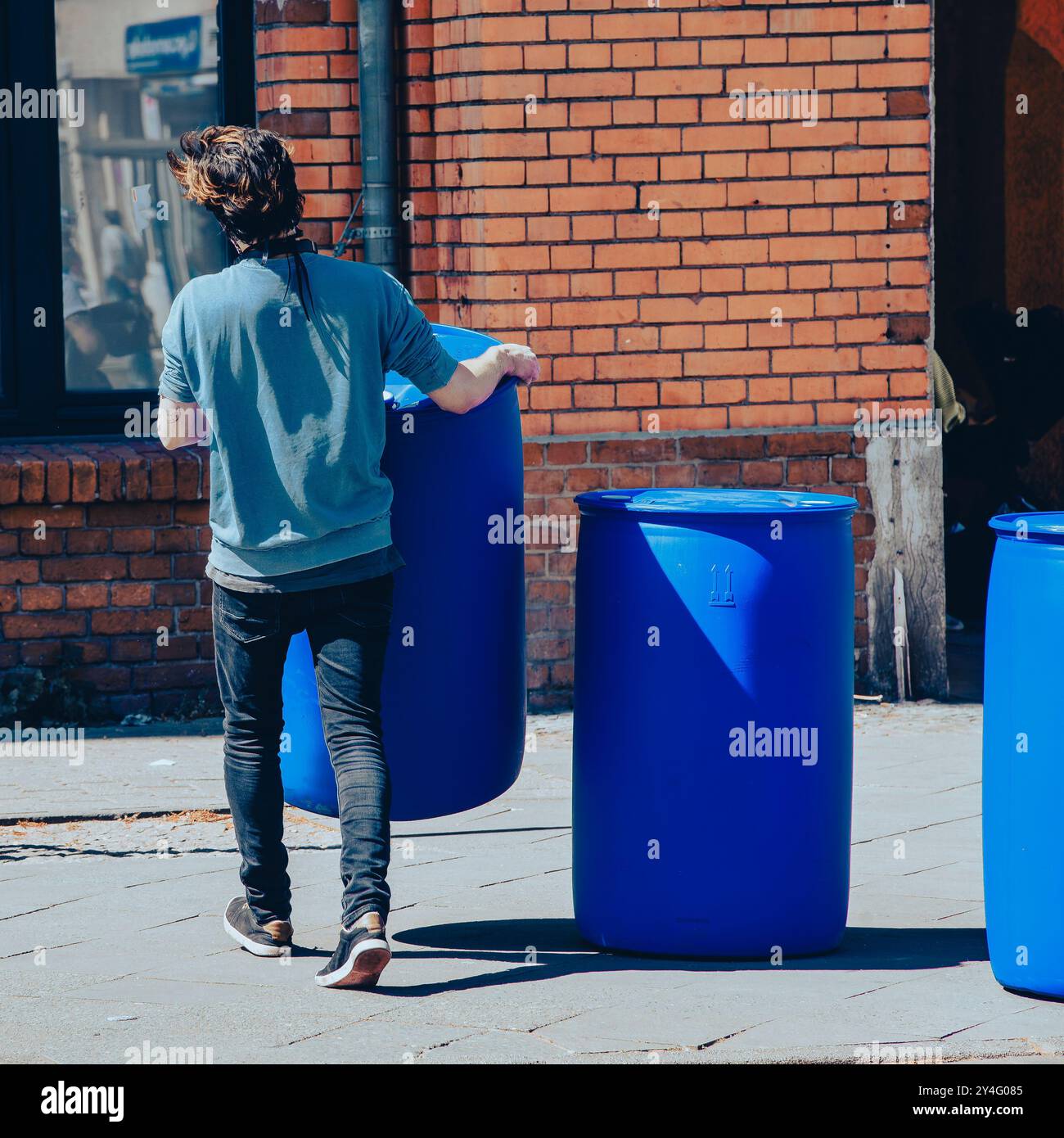 A young man carries a large blue barrel, several blue barrels in the ...