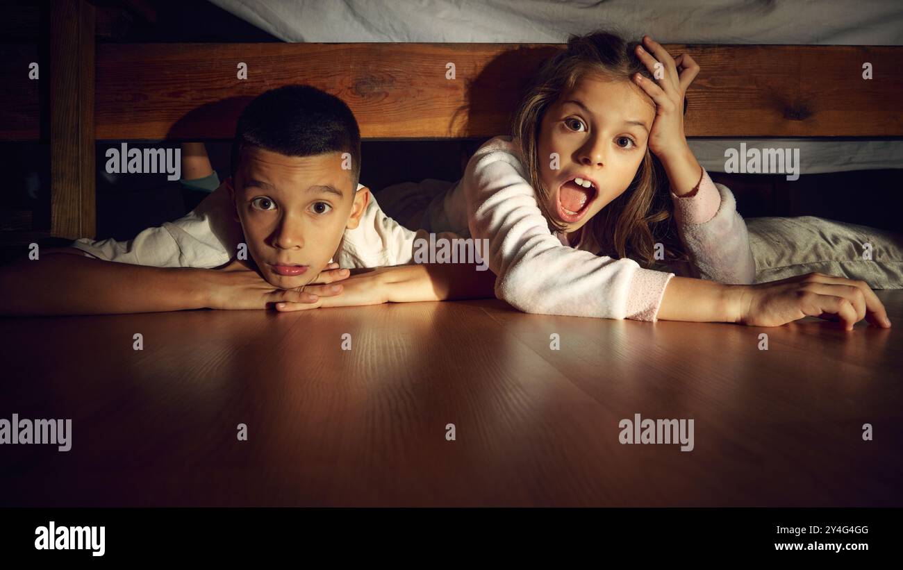 Two emotional kids, boy and girl peeking out bed with shocked faces ...