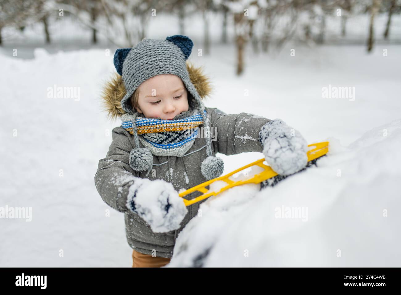 Adorable little boy helping to brush a snow from a car. Mommy's little ...