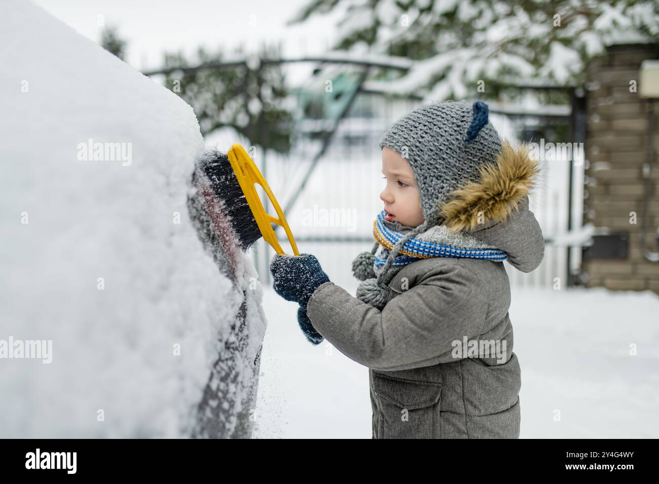 Adorable little boy helping to brush a snow from a car. Mommy's little ...