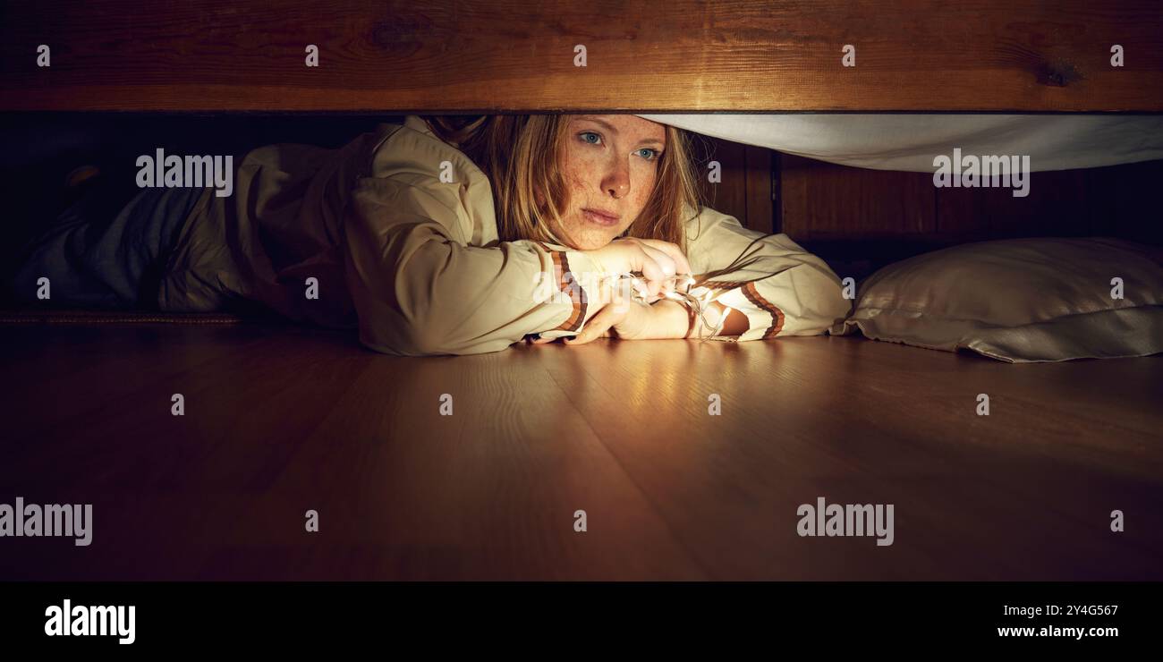 young woman lying under bed with pillow, feeling comfortable and safe ...