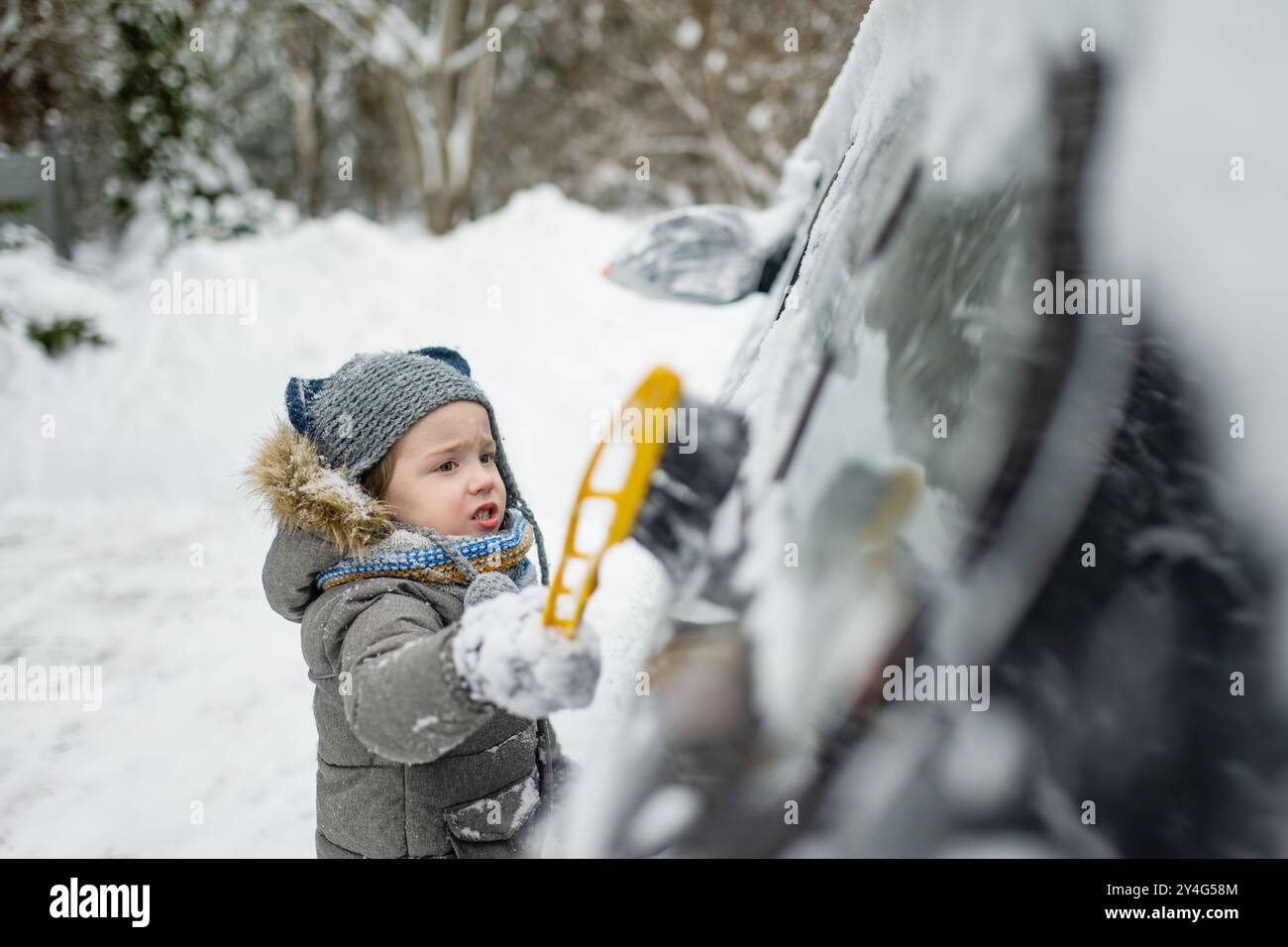 Adorable little boy helping to brush a snow from a car. Mommy's little ...