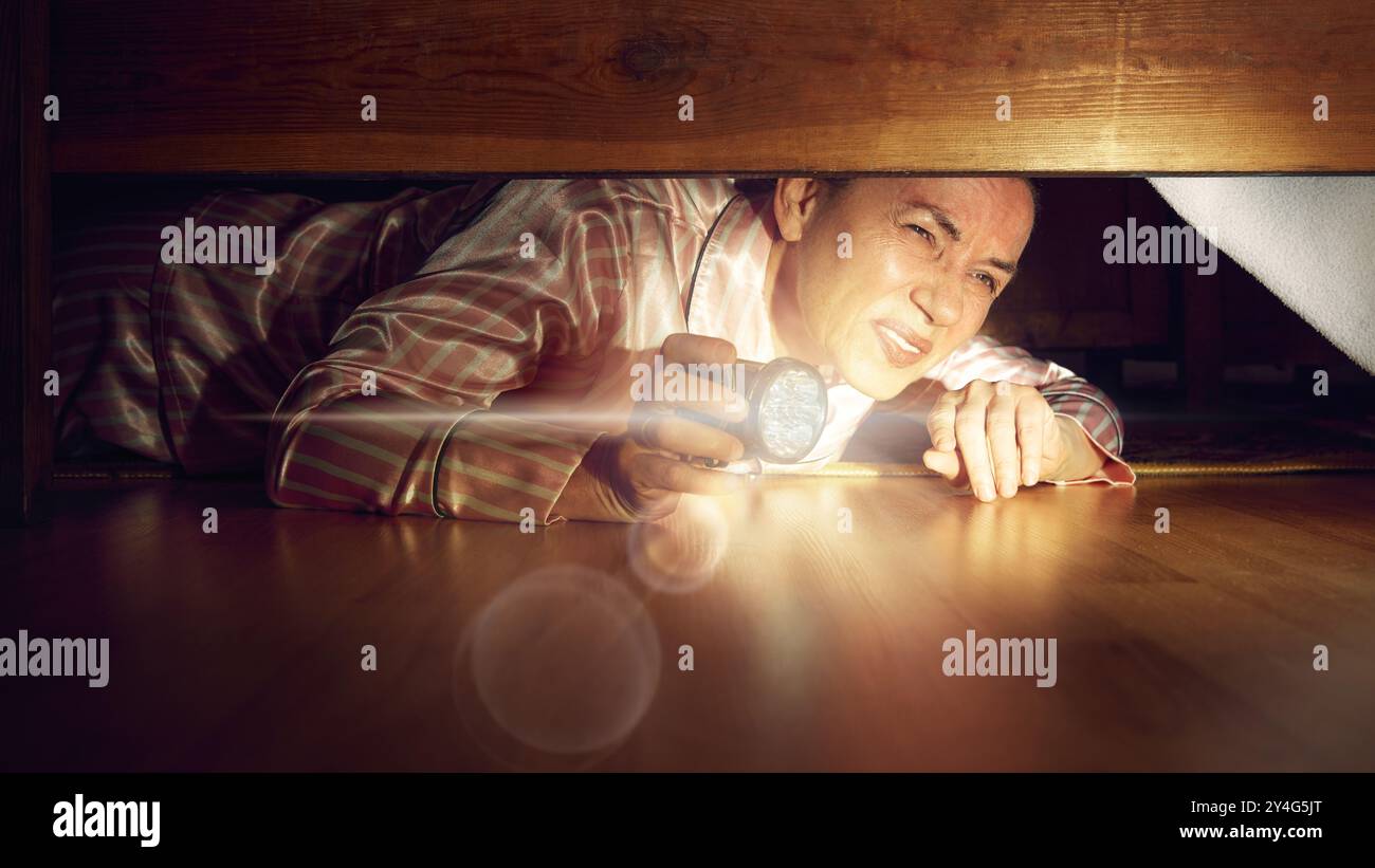 Emotional senior man looking under bed with flashlight, trying to find out something, Hidden ...